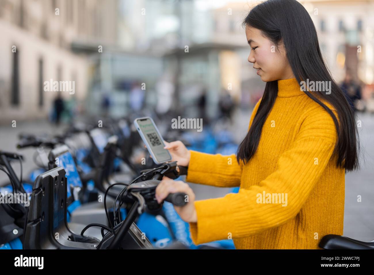 Young woman scanning QR code through smart phone and renting electric ...