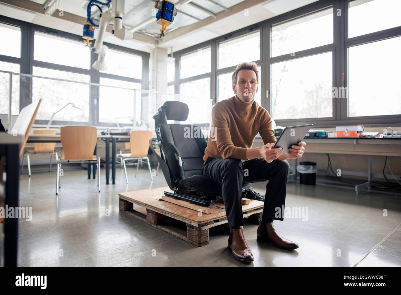 Engineer holding tablet PC sitting on chair attached over pallet at ...