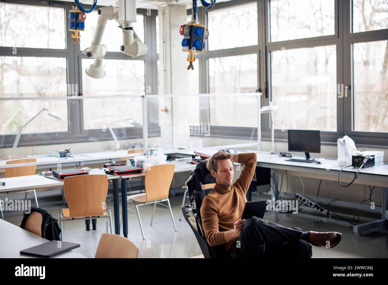 Engineer using tablet PC sitting on chair at workshop Stock Photo - Alamy