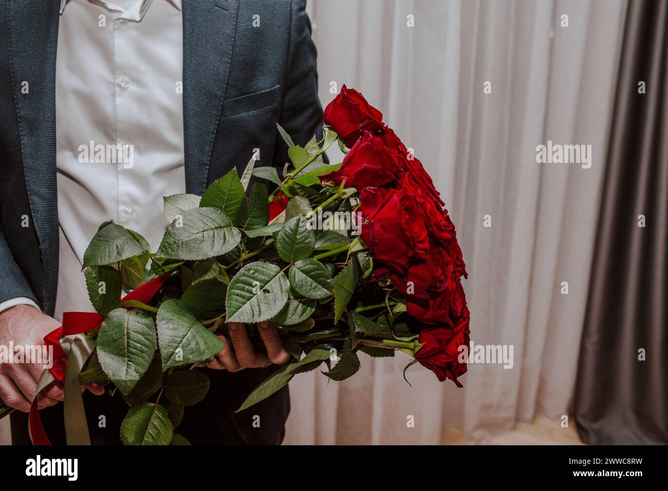 Boy wearing suit and holding bouquet of red roses at home Stock Photo ...