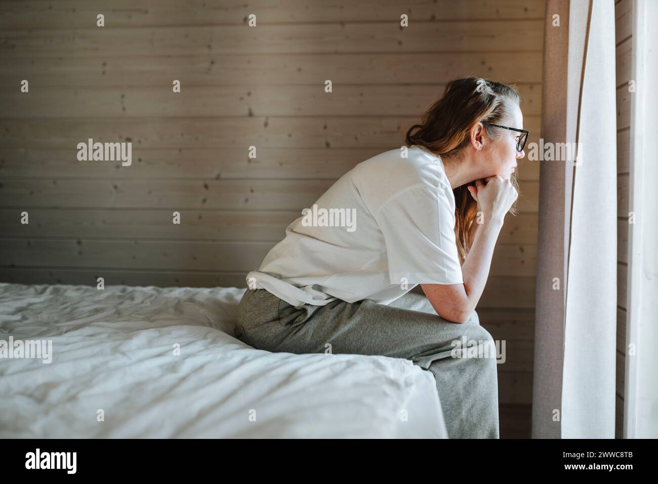 Stressed woman leaning on elbows and looking out of window at home ...