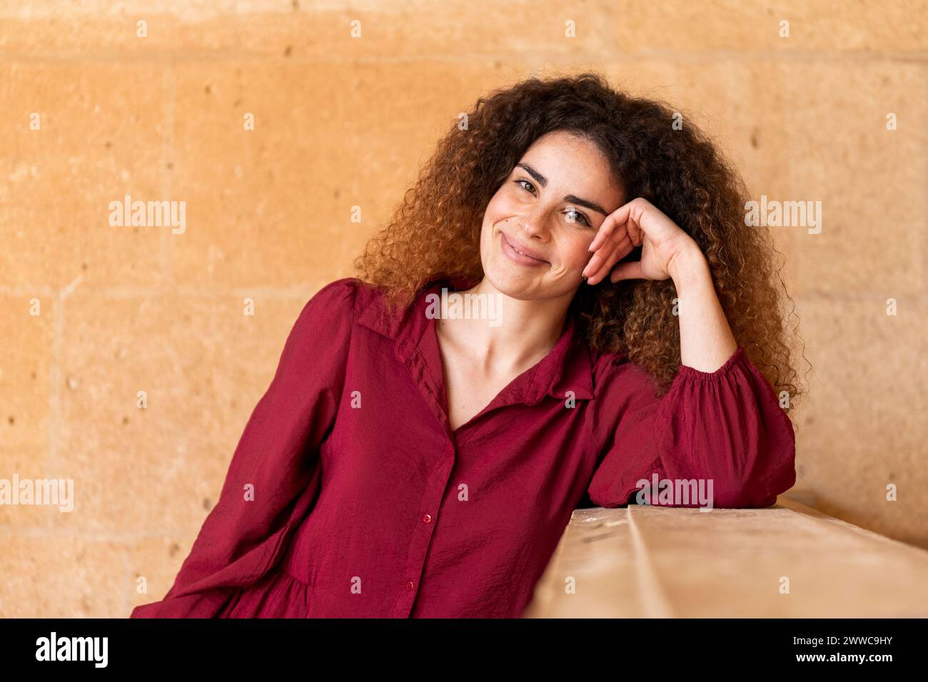 Smiling woman with curly hair leaning on elbow in front of wall Stock ...