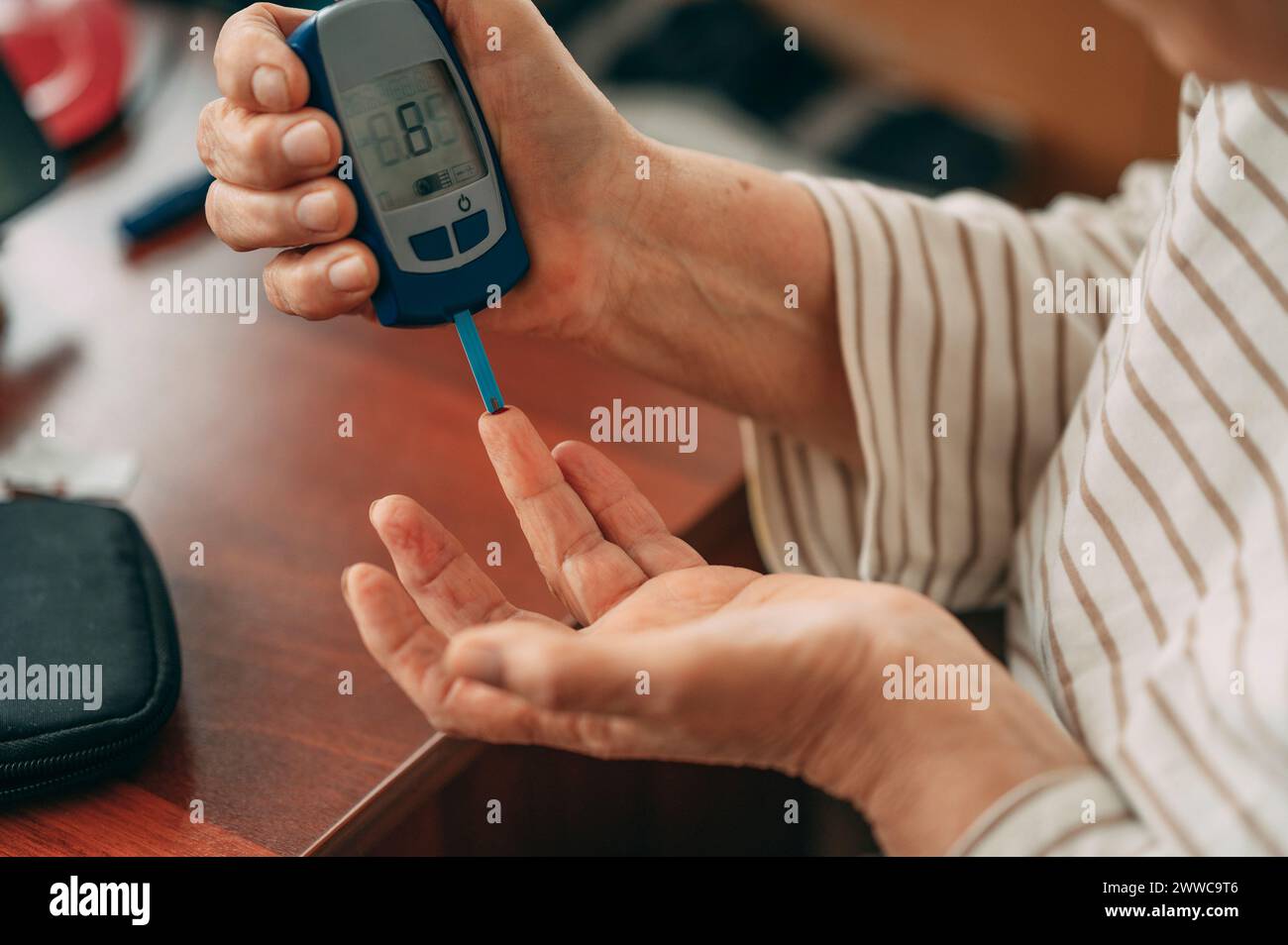 Senior woman measuring blood sugar level through glucometer at home ...