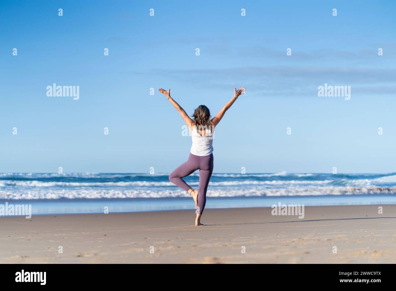 Woman doing tree yoga pose with arms raised at beach Stock Photo - Alamy