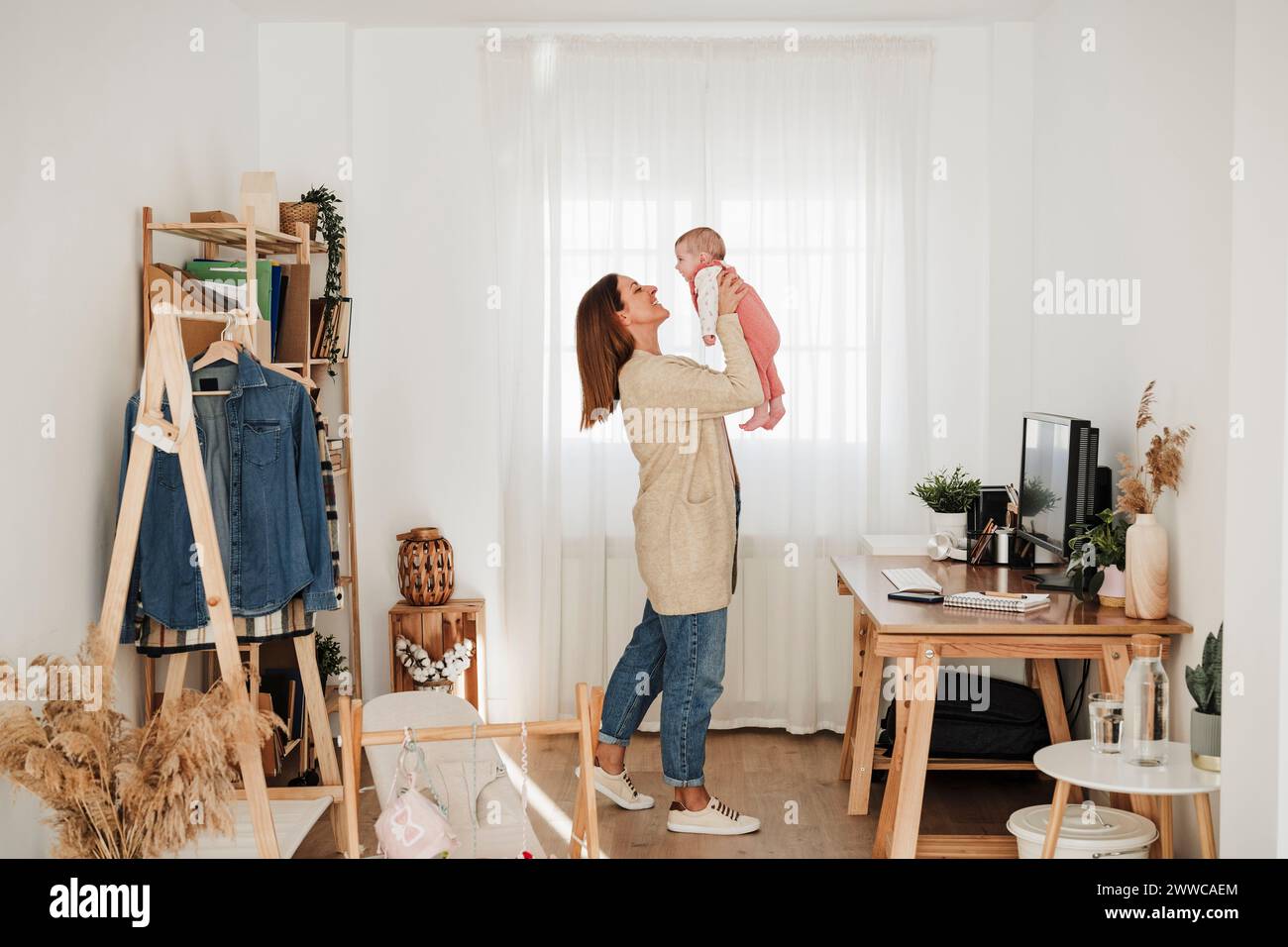 Mother picking up baby daughter standing in home office Stock Photo - Alamy