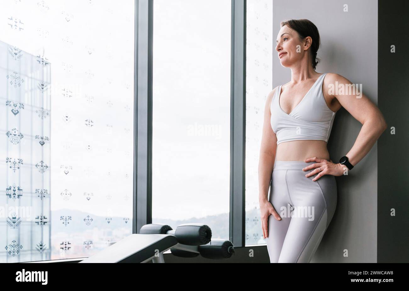 Woman standing with hand on hip and looking through window at gym Stock ...