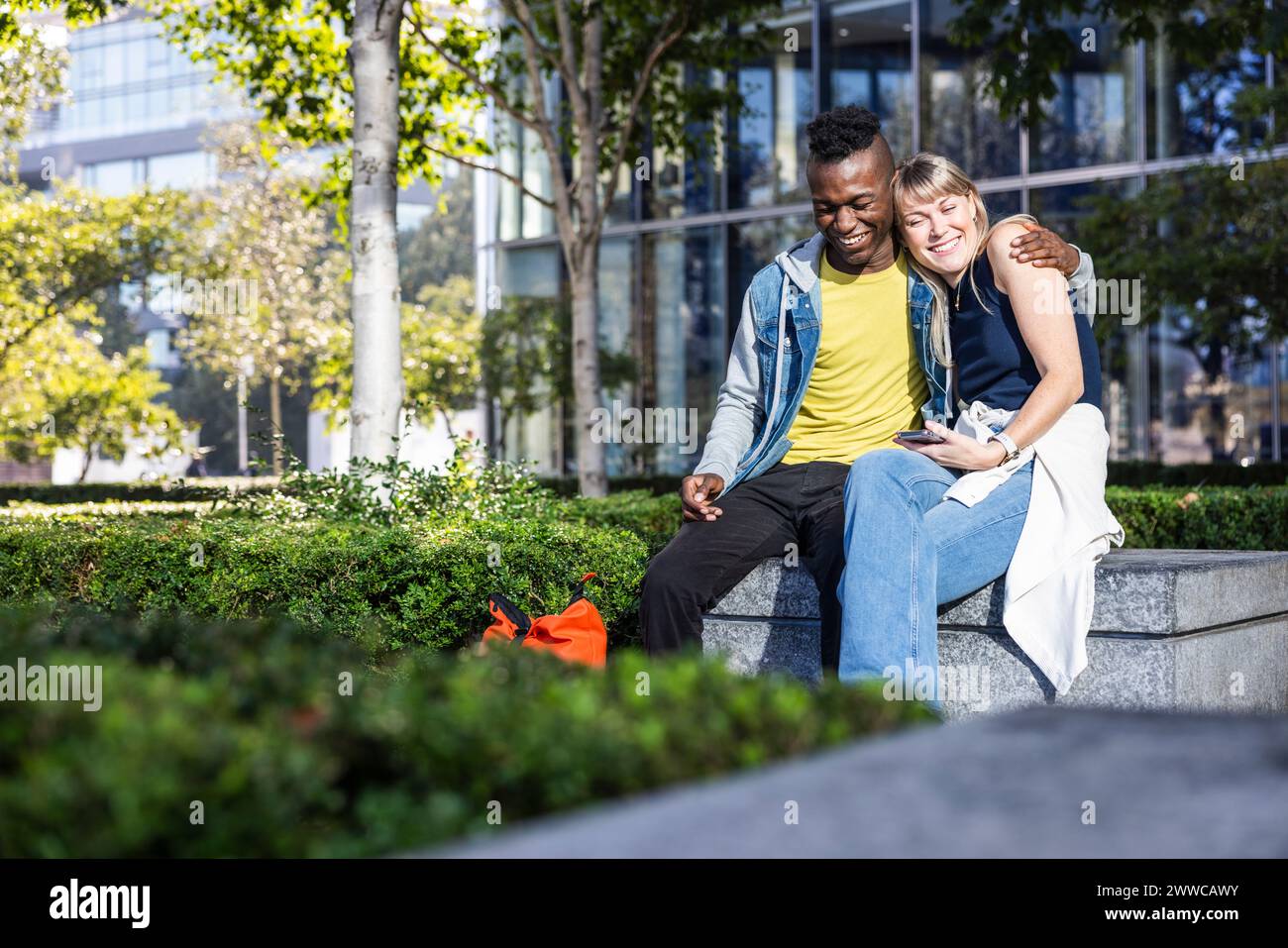 Smiling man sitting with arm around friend on bench at park Stock Photo ...