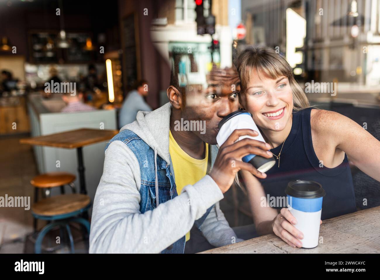 Curious multiracial friends drinking coffee and looking out of window ...