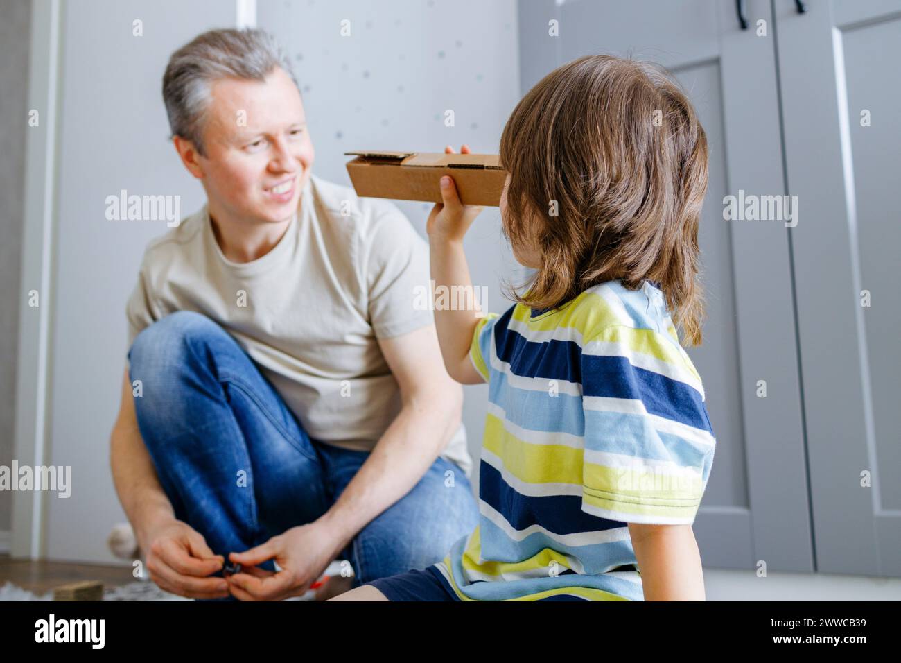 Boy looking at father through box in home Stock Photo - Alamy