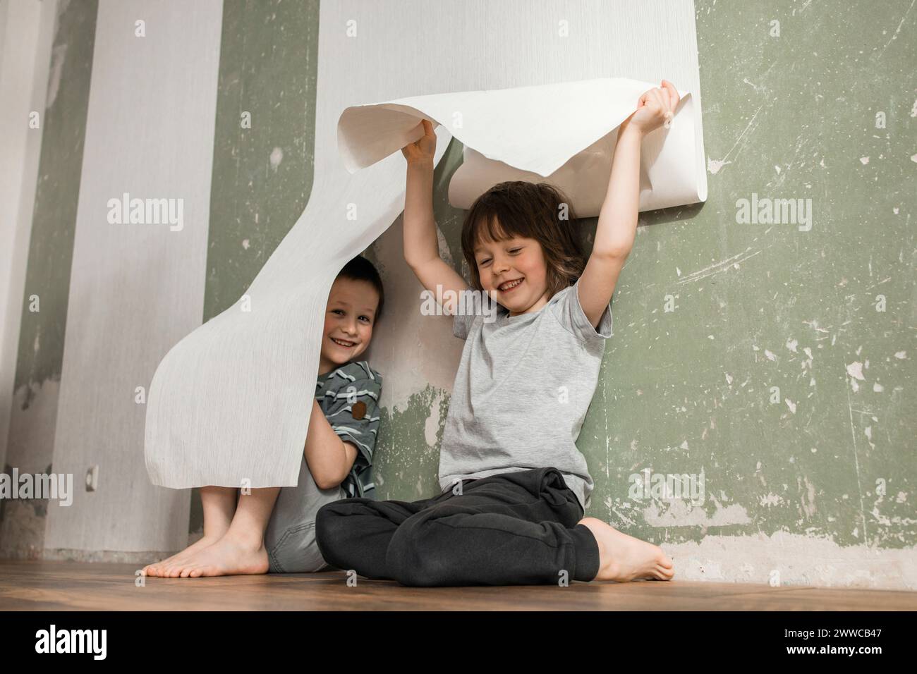 Cheerful brothers hiding under white wallpaper at home Stock Photo - Alamy