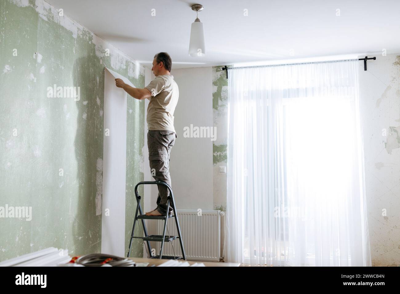 Man on step ladder gluing wallpaper in living room at home Stock Photo ...