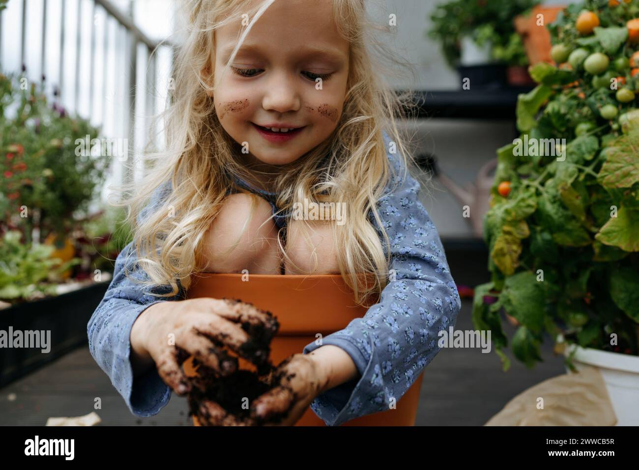 Smiling girl sitting with handful of dirt in pot at balcony Stock Photo ...