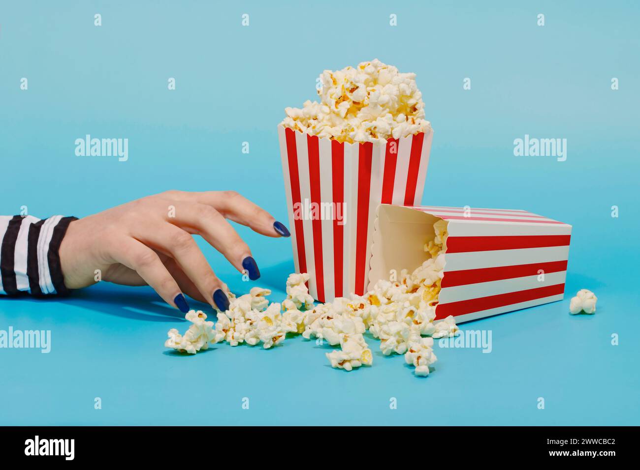 Hand of woman reaching for popcorn over blue background Stock Photo - Alamy