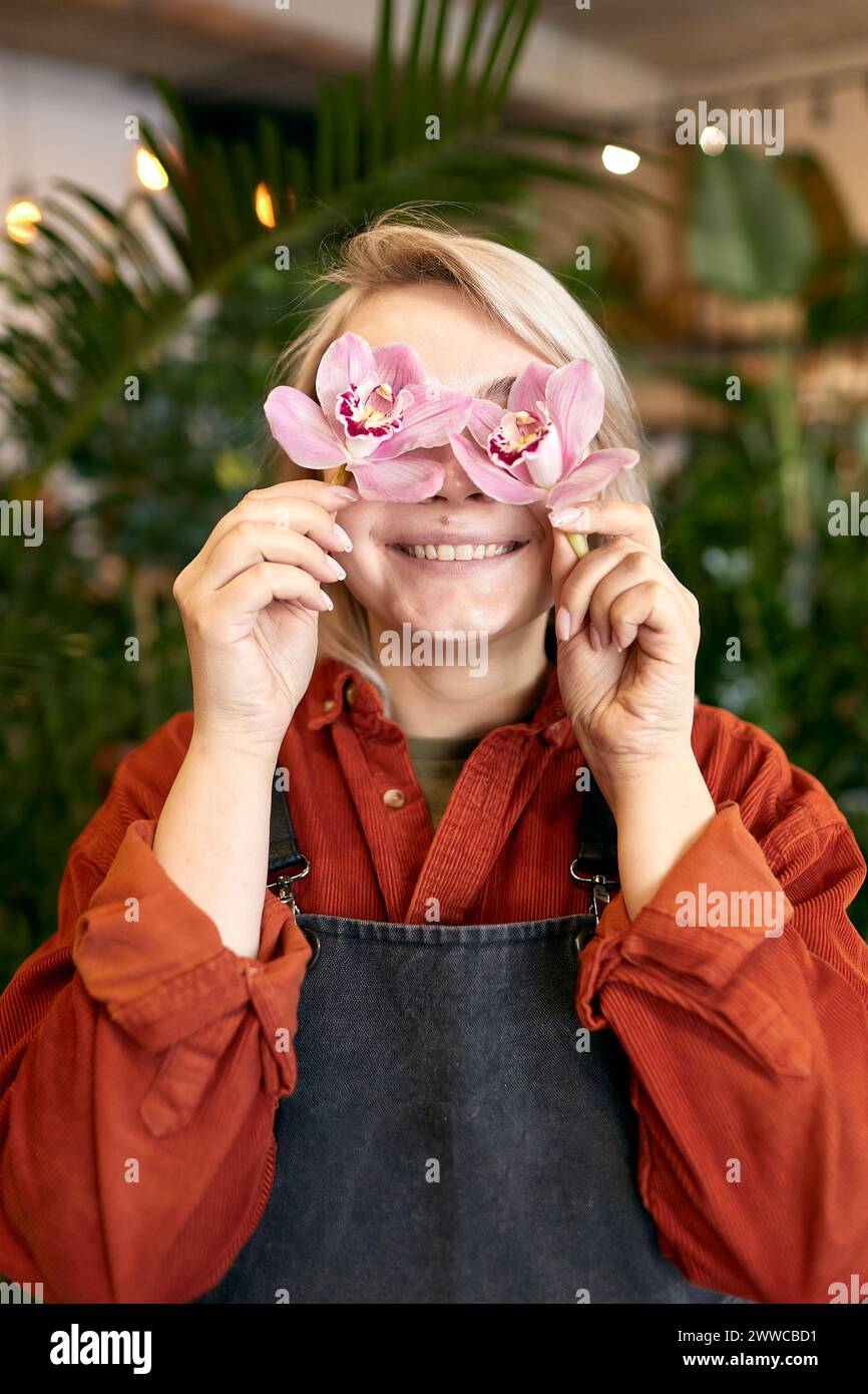 Smiling florist holding pink colored flowers over eyes Stock Photo - Alamy