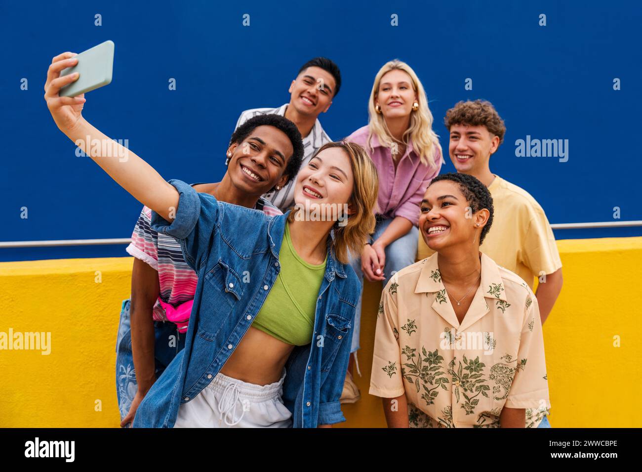 Group of friends friends with colorful clothing sitting on yellow wall ...