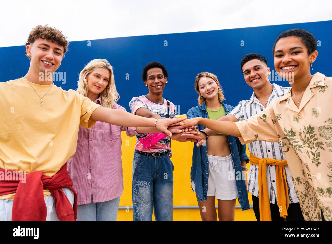 Multi-ethnic group of young friends stacking hands in front of wall ...