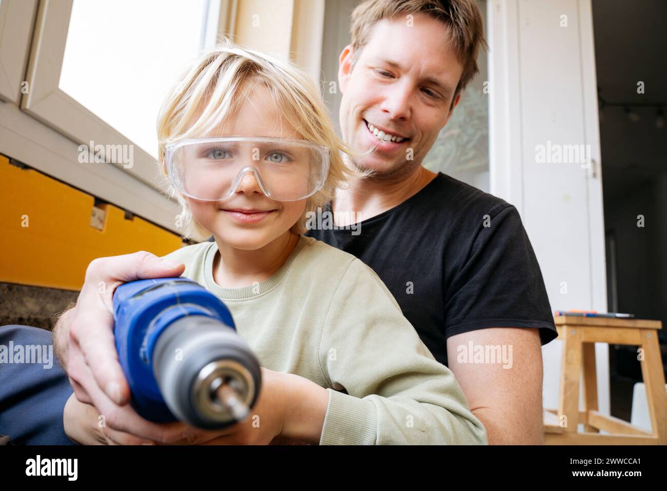Smiling son and father holding drill machine at home Stock Photo - Alamy