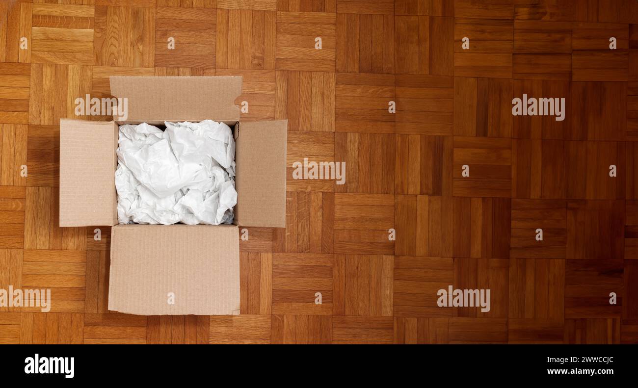 Cardboard box filled with shipping packaging paper on a wood floor ...