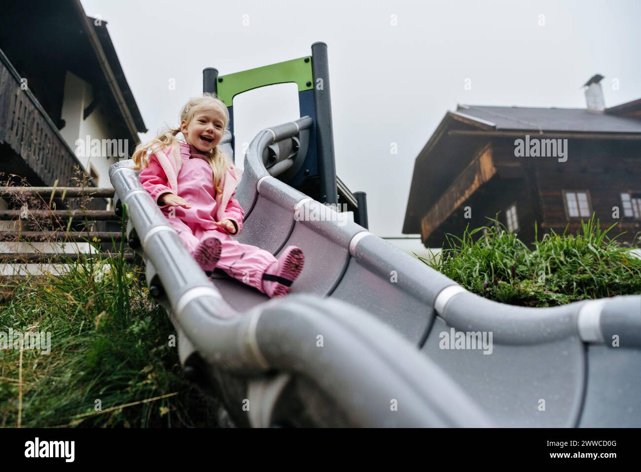 Girl in pink raincoat sliding down slide at playground Stock Photo - Alamy