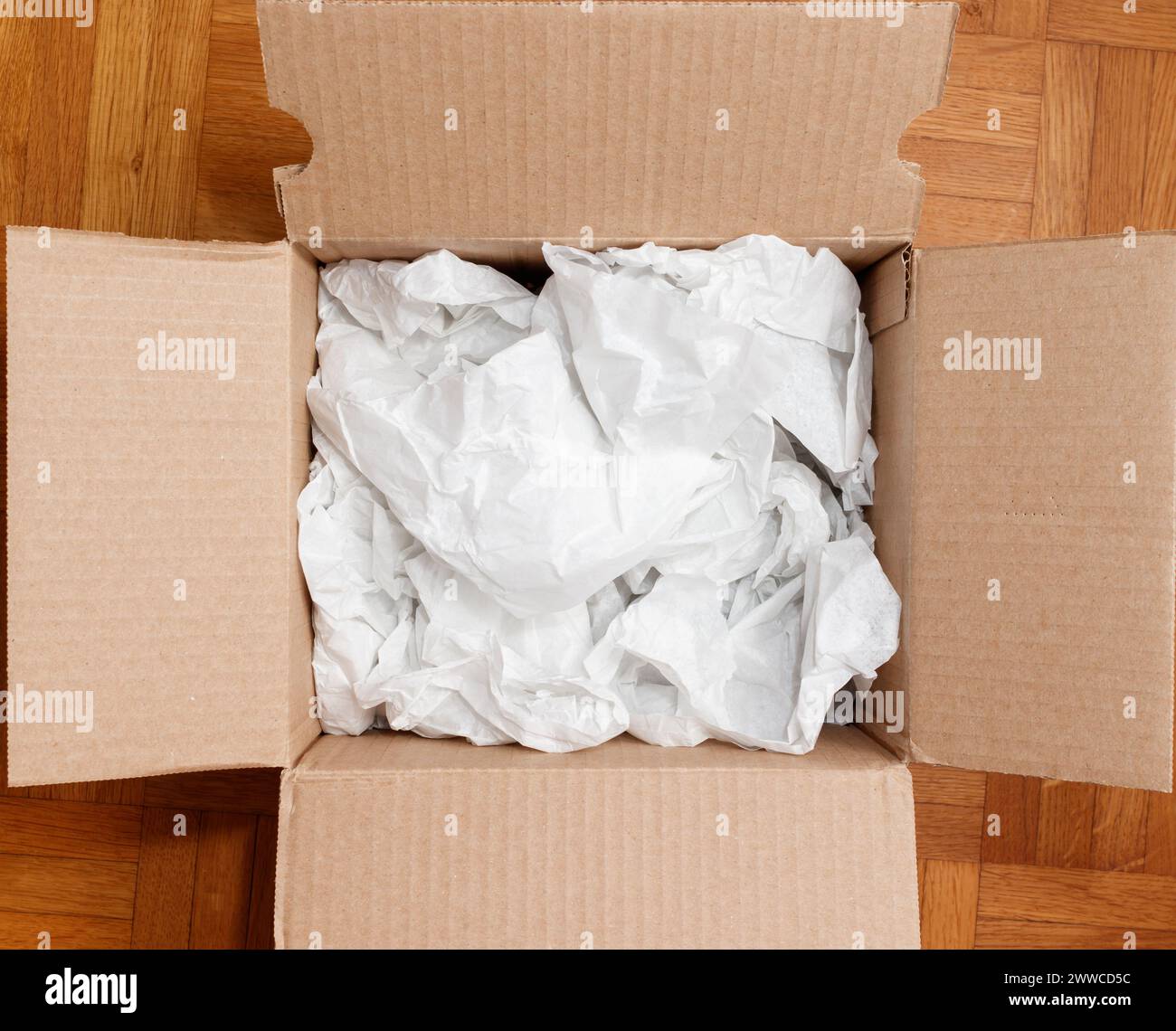 Cardboard box filled with shipping packaging paper on a wood floor ...