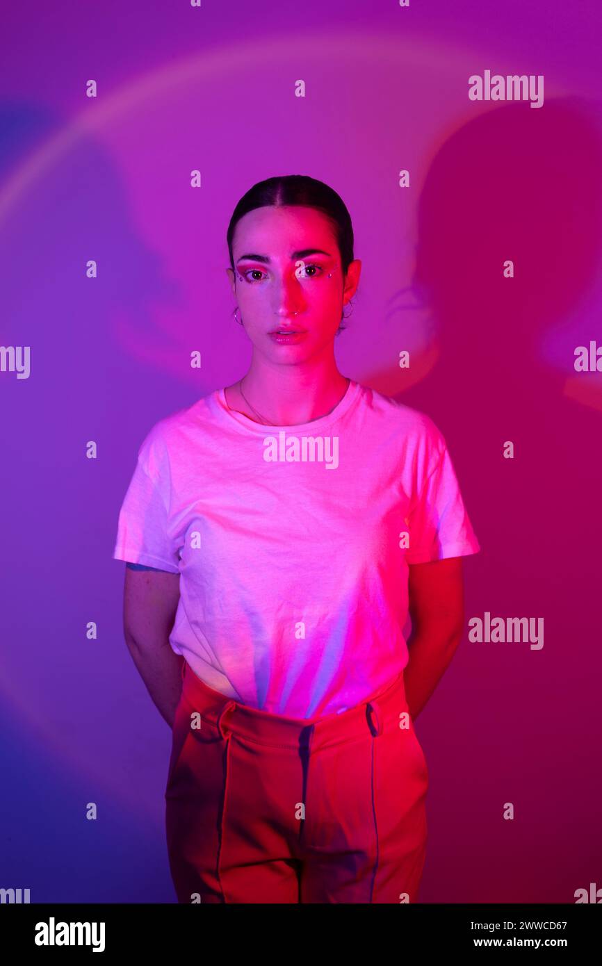 Young woman with hands behind back in neon lighting against gradient ...