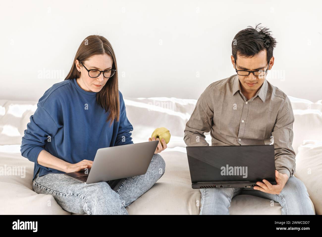 Diverse programmers using laptops sitting on sofa at creative startup ...