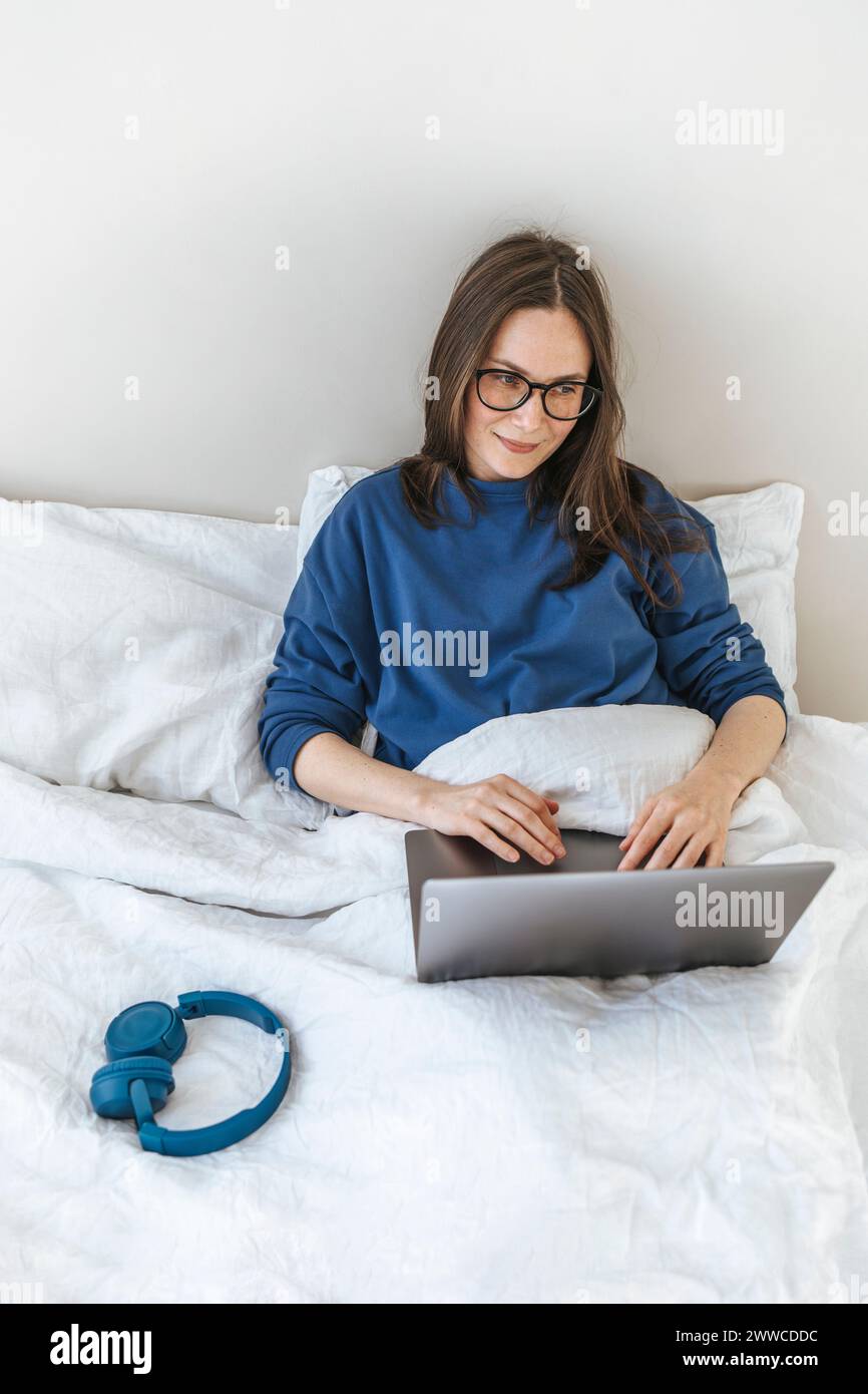 Smiling programmer coding through laptop sitting on bed at home Stock ...