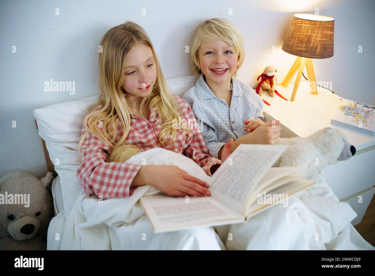 Happy siblings reading book sitting on bed at home Stock Photo - Alamy