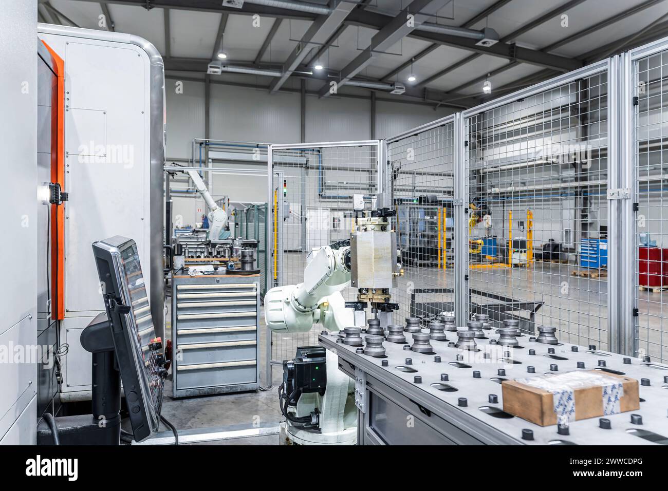 White robotic arm with CNC machinery in modern manufacturing building ...