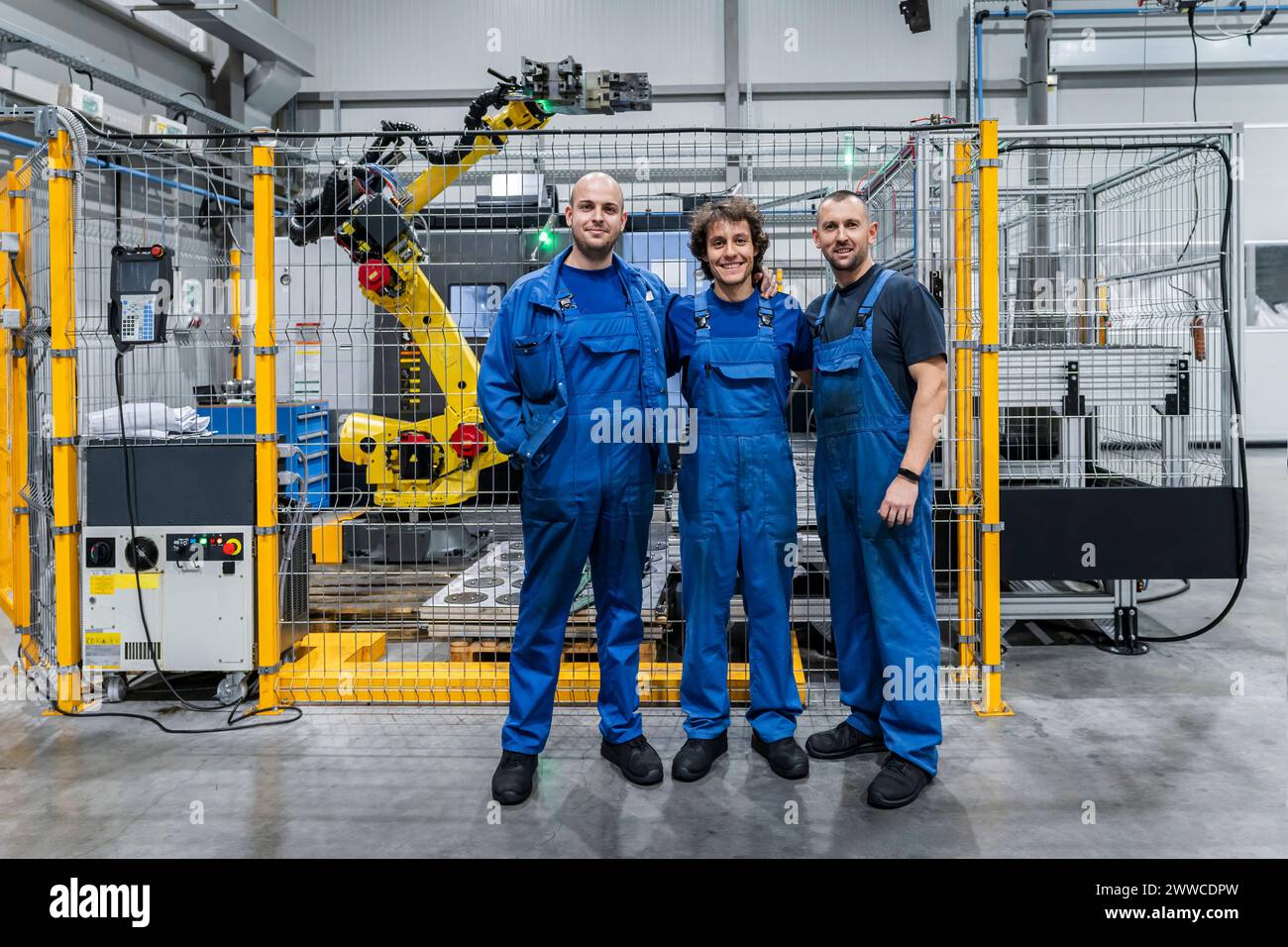 Smiling technician colleagues in front of machinery with robotic arm at ...