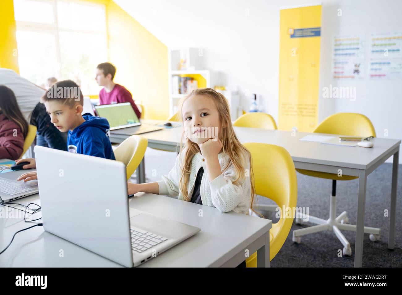 Girl sitting with hand on chin using laptop in computer classroom at ...