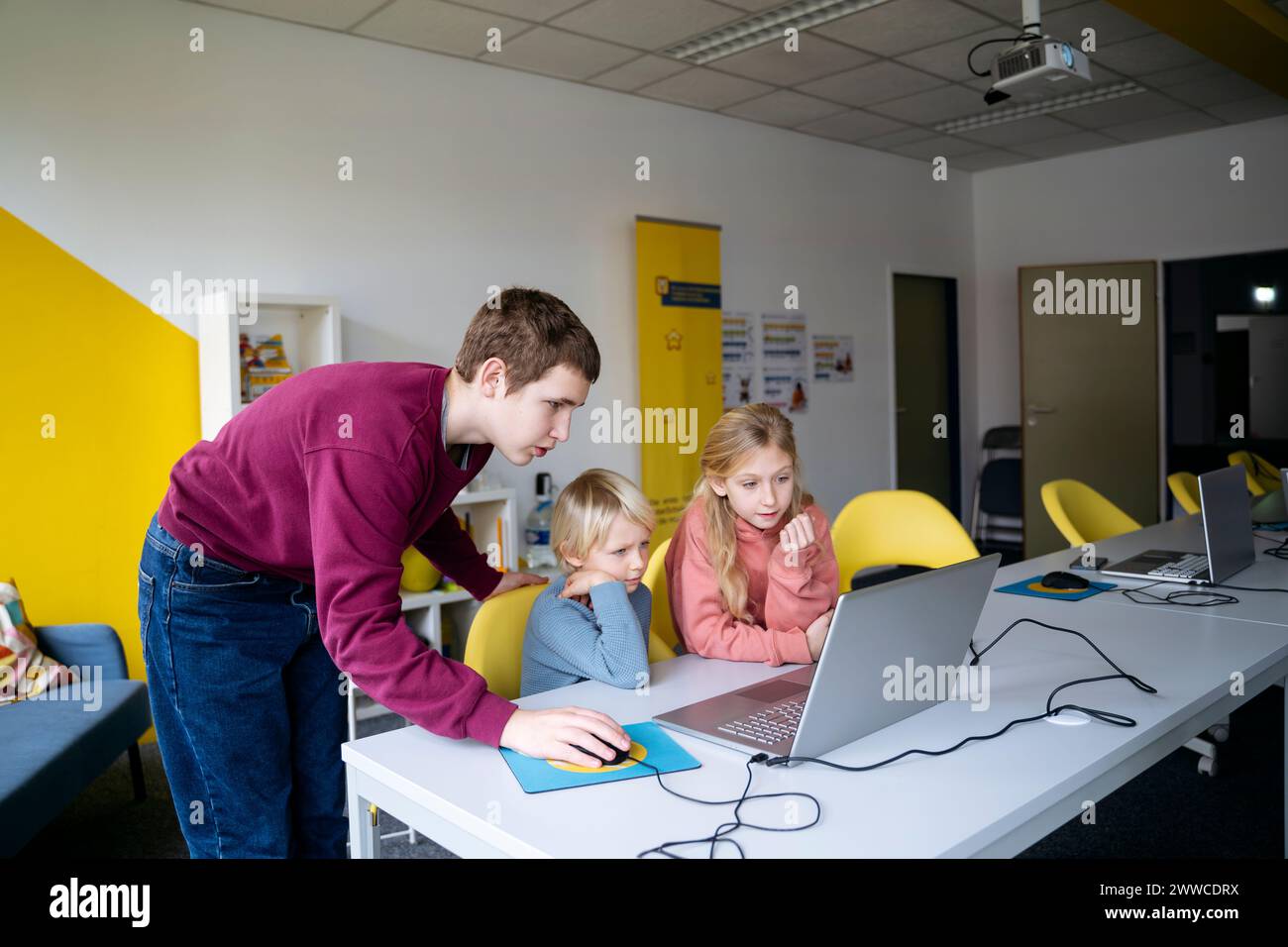 Teenage boy assisting students with coding in classroom Stock Photo - Alamy