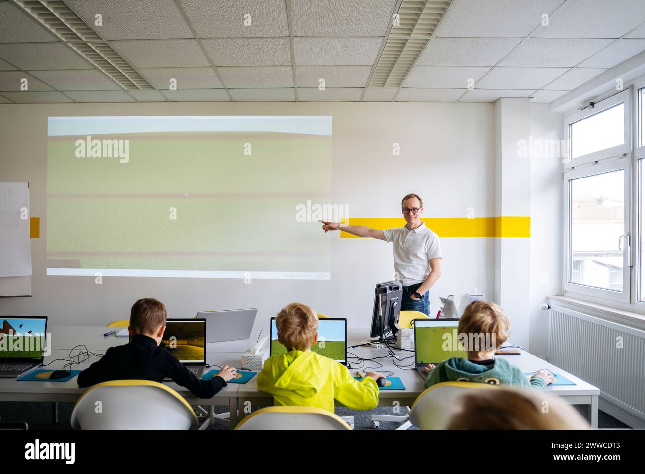 Professor pointing at projection screen and teaching computer to boys ...