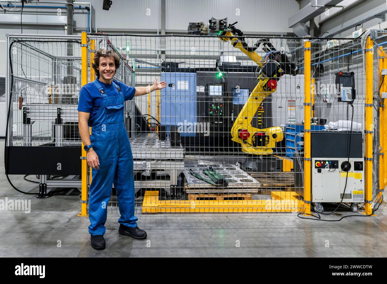 Smiling maintenance engineer gesturing at robotic arm in modern factory ...