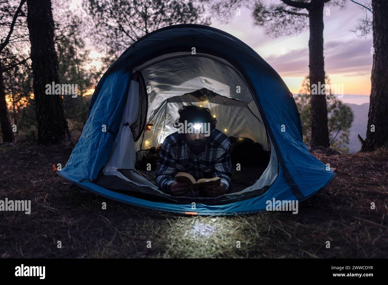 Man wearing headlamp and reading book in tent Stock Photo - Alamy