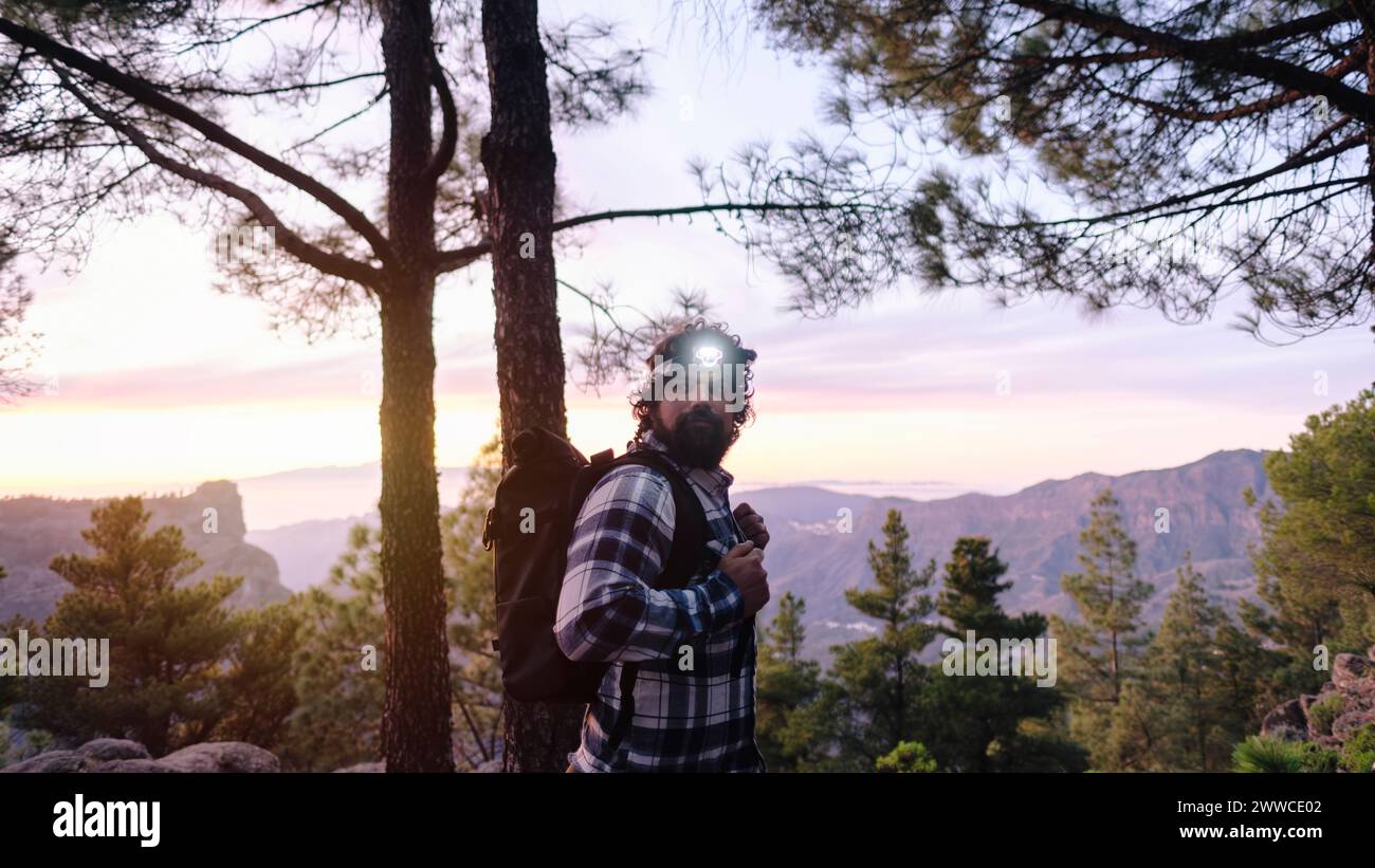 Man wearing headlamp and standing near trees in front of mountains ...