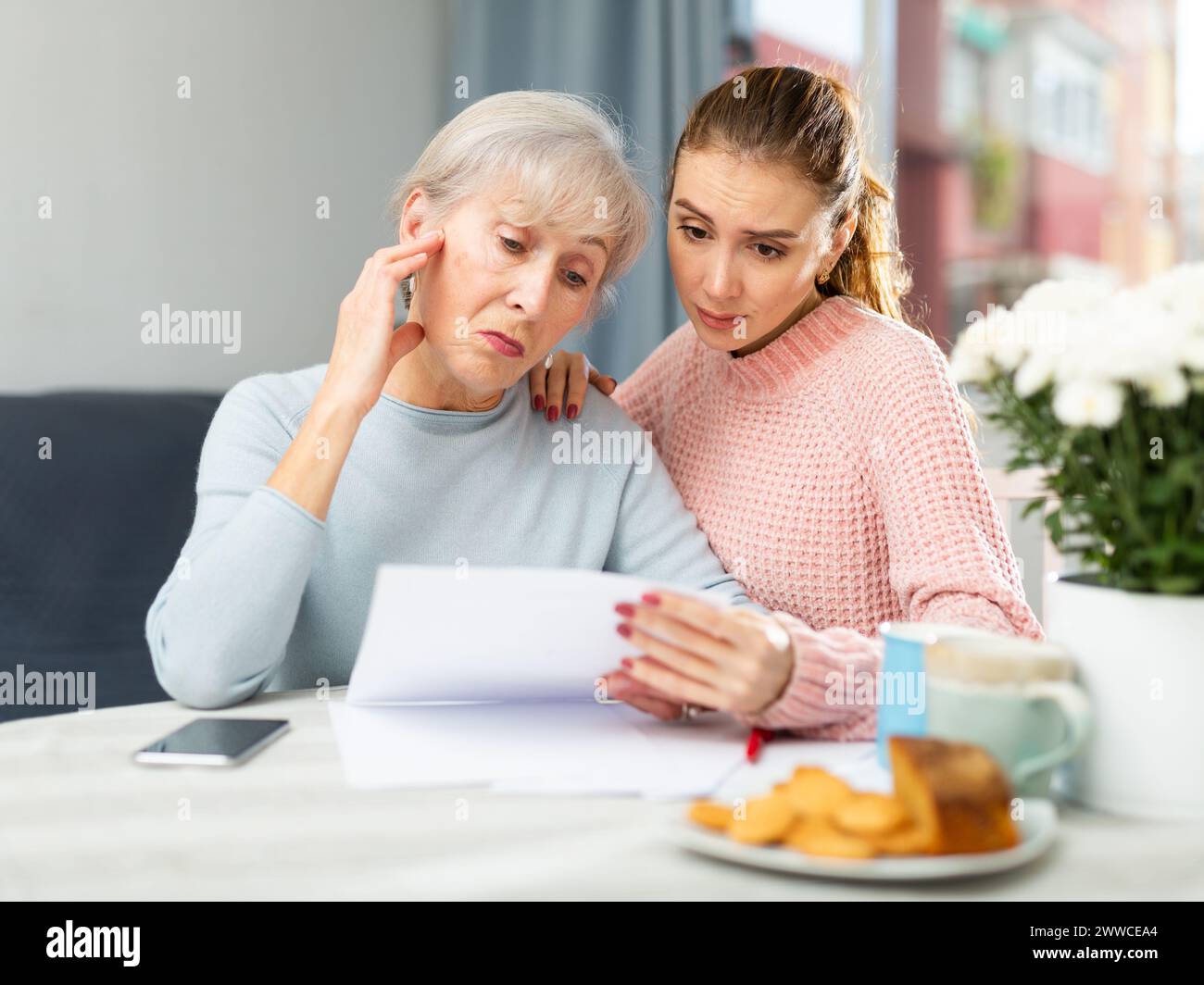 Upset young woman with aged mother looking worriedly at papers at home ...
