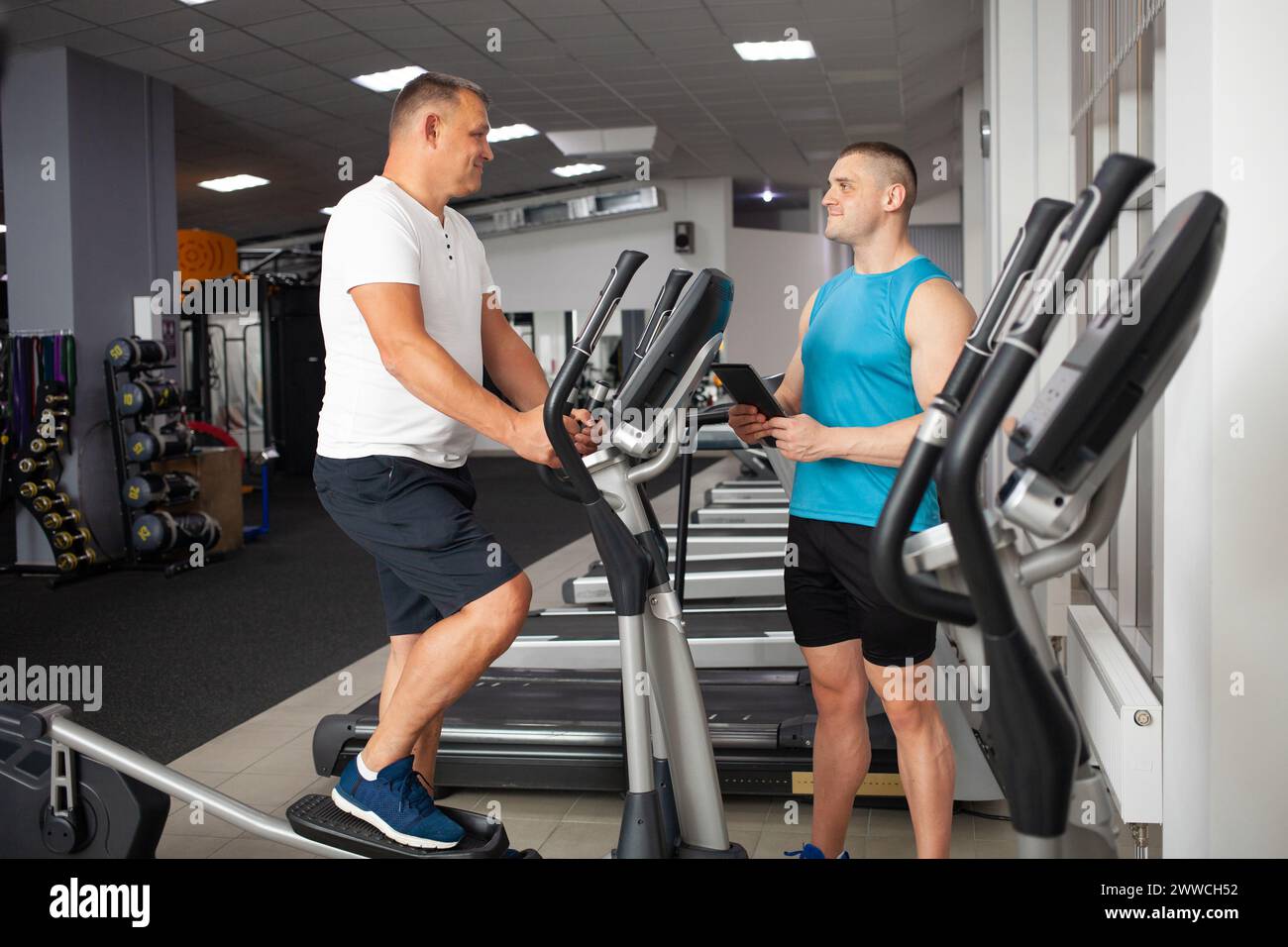 Men perform exercises in the gym. Coach and fat client, model size plus ...