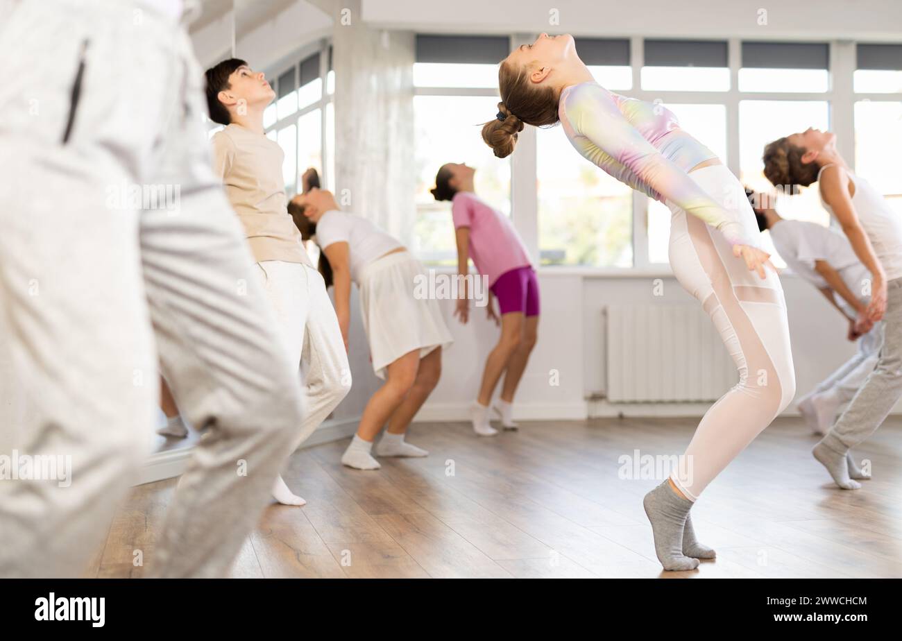Female girl student repeats movements of unrecognizable teacher during group modern dance class ...