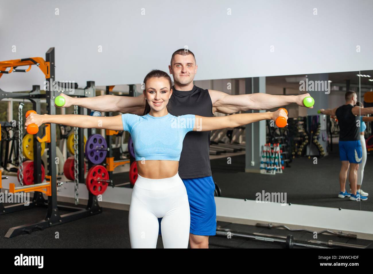 beautiful fitness trainers smile, do exercise with dumbbells in the gym ...