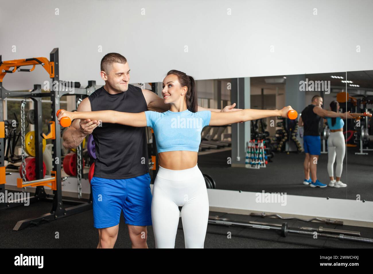 beautiful fitness trainers smile, do exercise with dumbbells in the gym ...