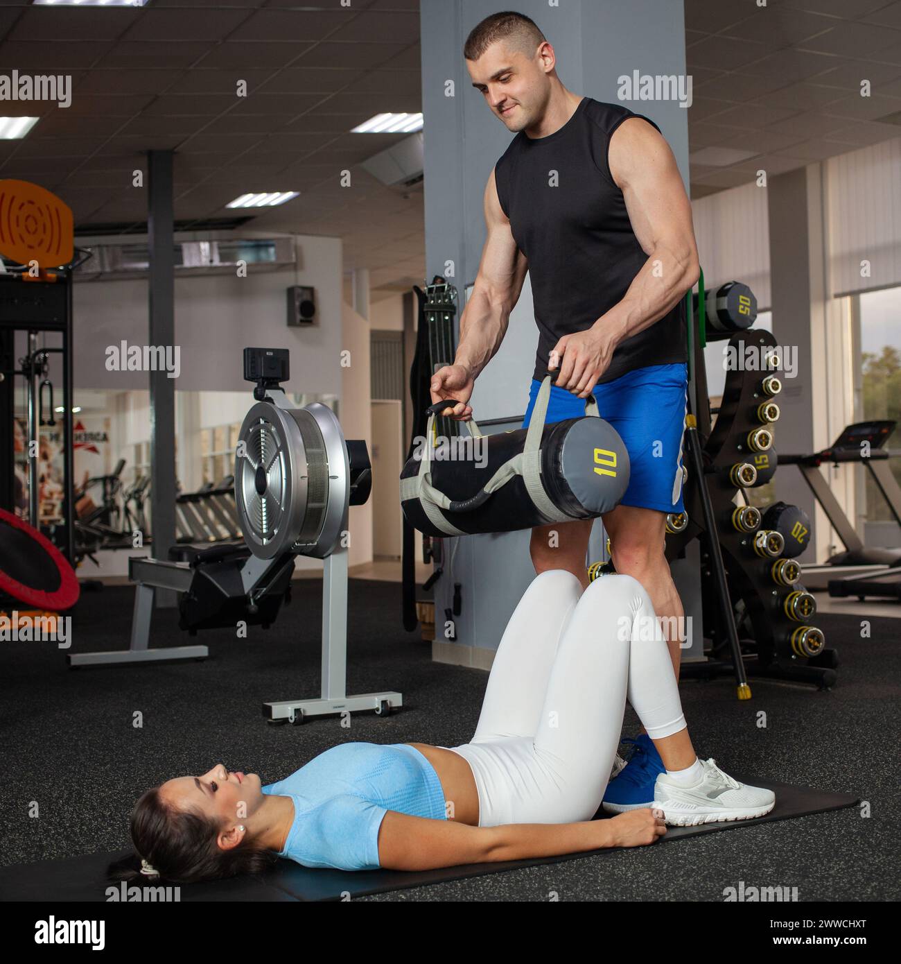 the trainer helps the woman to perform the exercise with a weighting ...