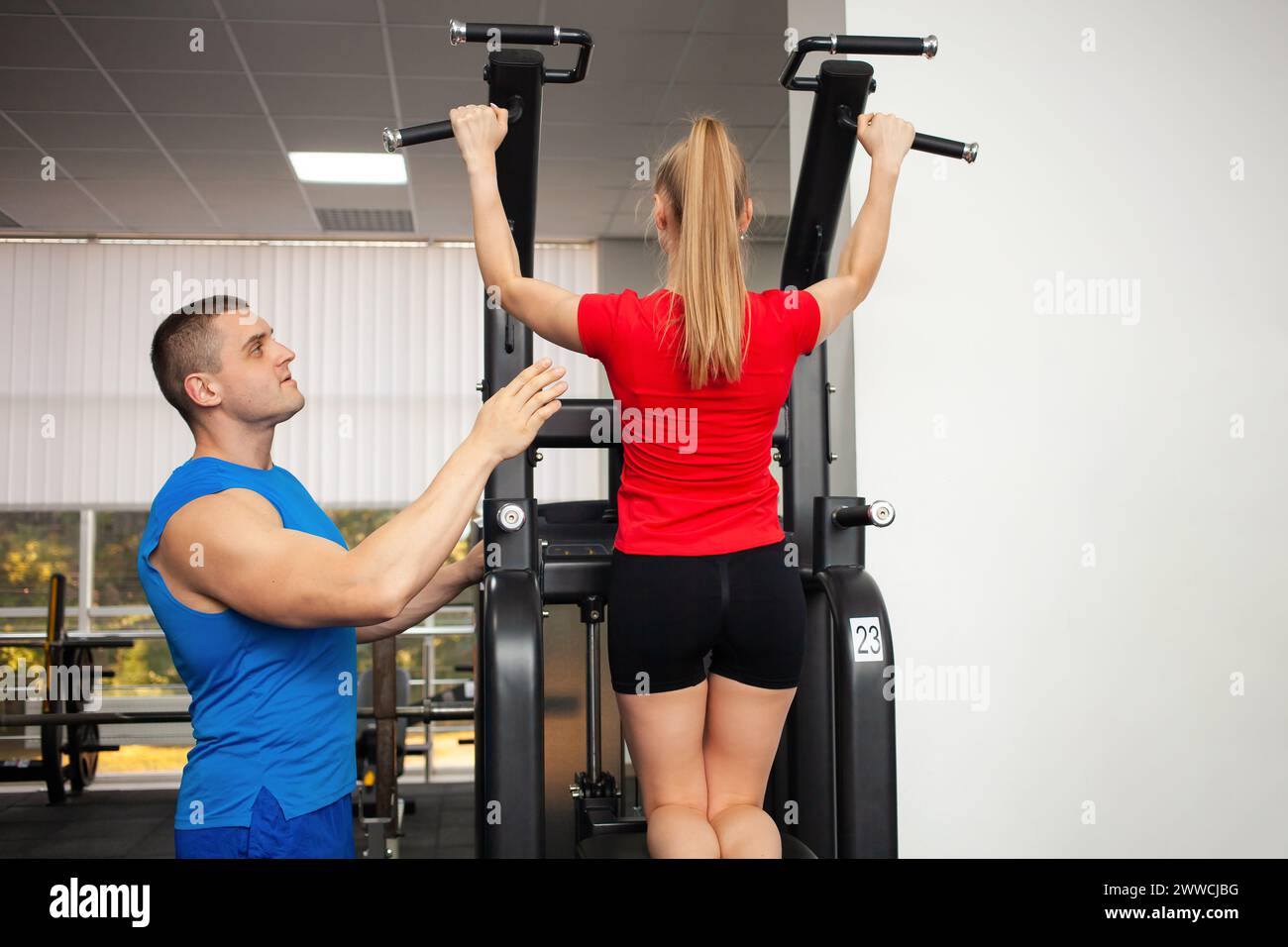 teenager performs exercise on simulator. Gym, muscles on back. coach ...