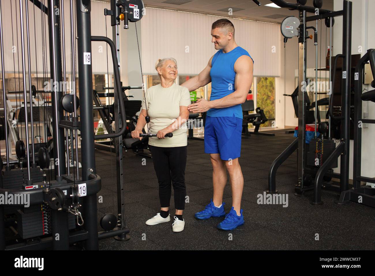 young handsome coach man helps a pensioner to do an exercise on the ...