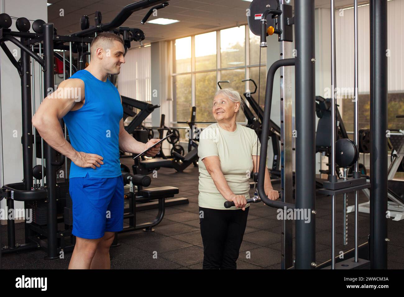 A young handsome coach man helps a pensioner to do an exercise on the ...
