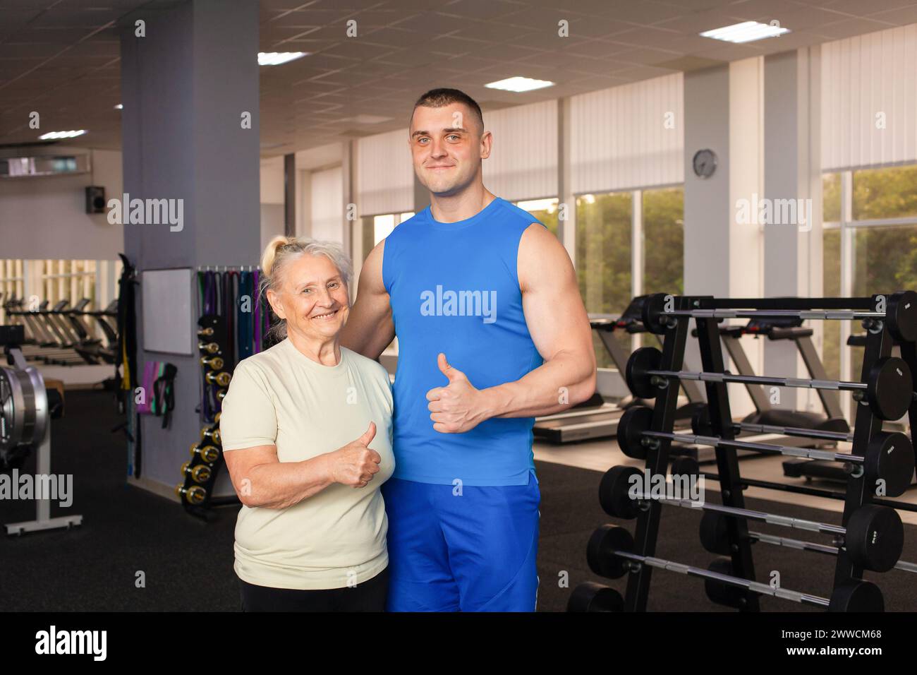 Portrait of a young coach in uniform and an old woman in gym. Physical ...