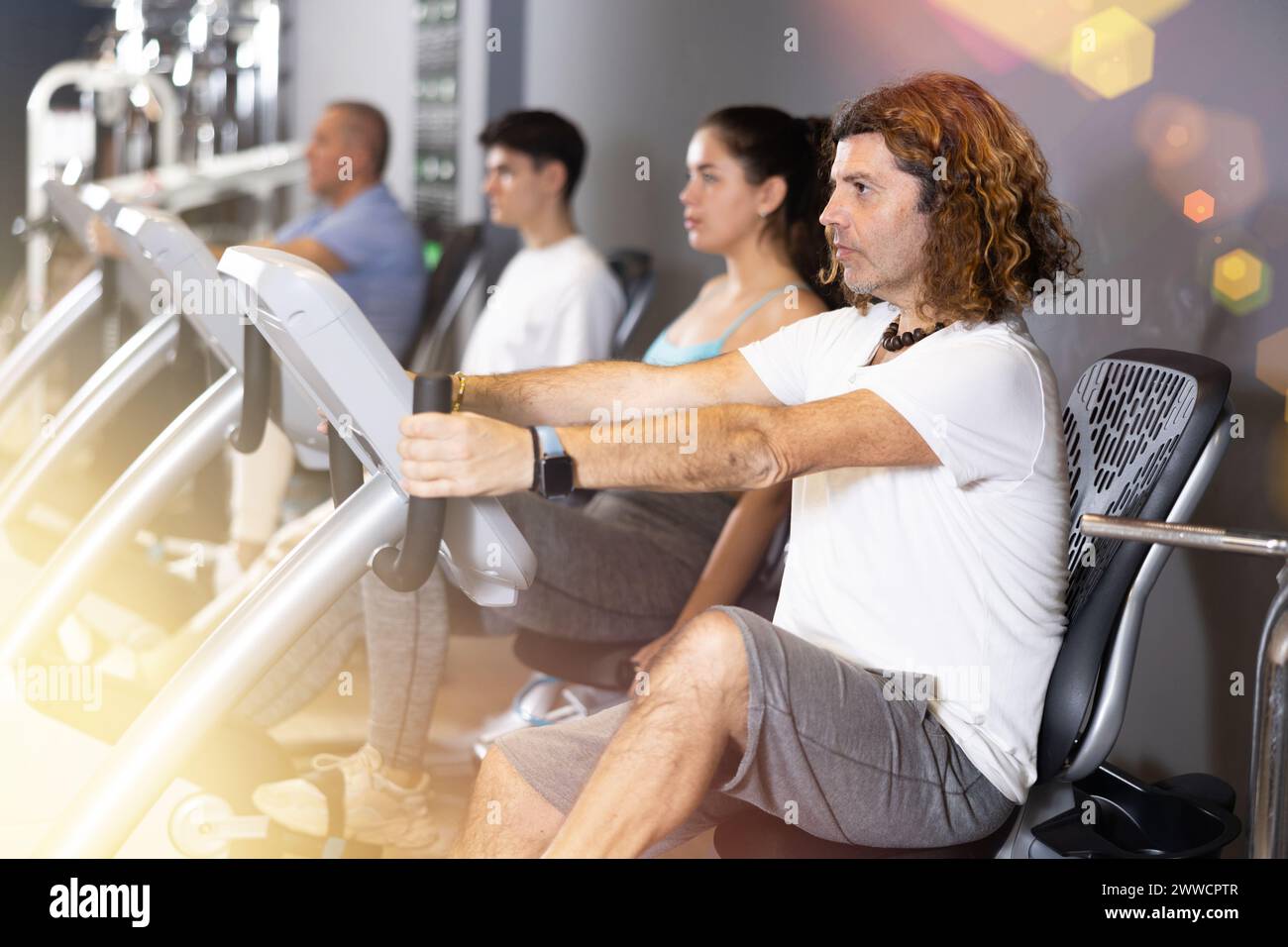 Group of people of different ages are engaged in cardio equipment in ...