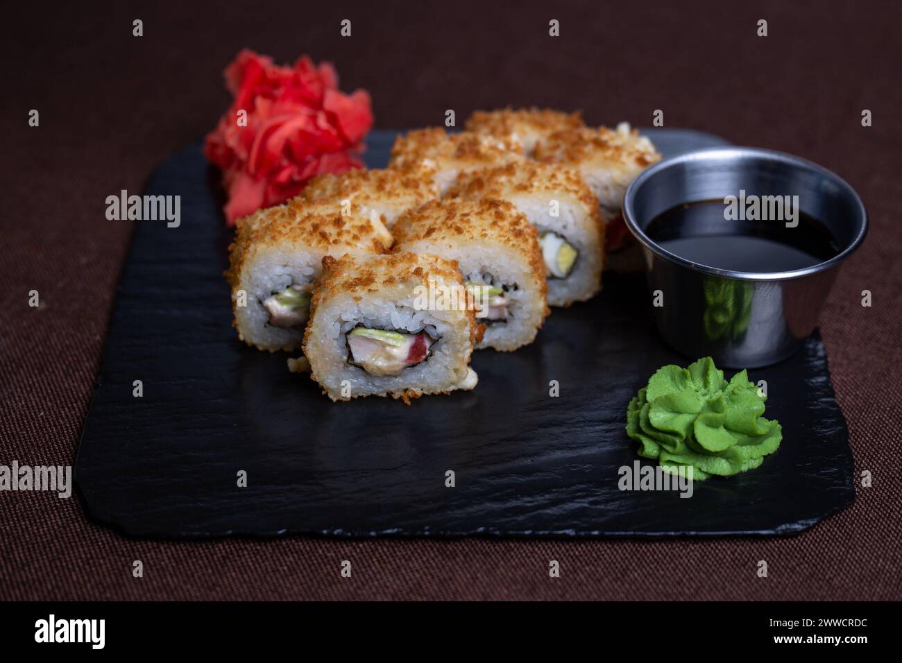 Deep-fried sushi roll on black stone plate with soy sauce, wasabi. Made ...