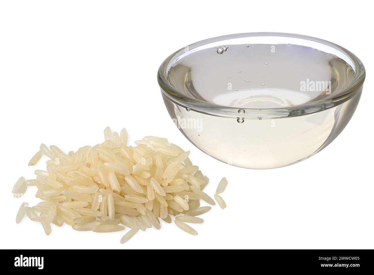 Rice syrup in a glass bowl next to a pile of uncooked white rice ...