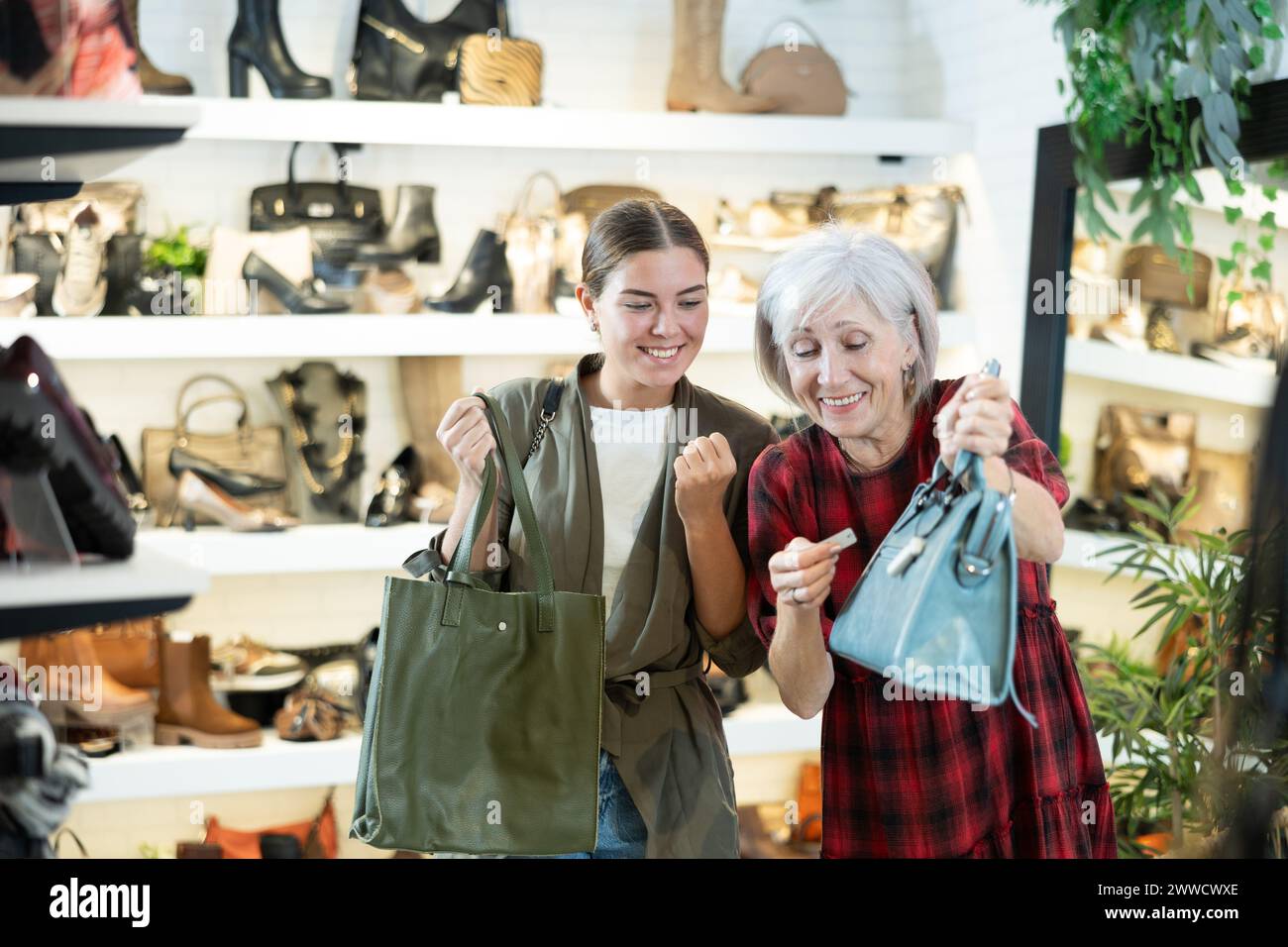 Two cheerful female shoppers discussing models of handbags in store ...